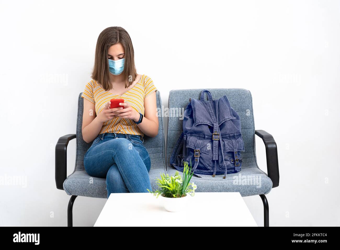 A young female client in the waiting room with a mask browsing on the ...