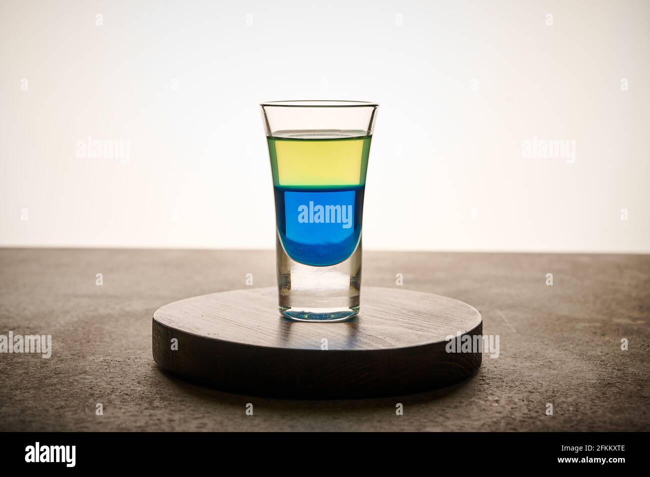 Homemade yellow and blue transparent alcohol drink in glass of ...