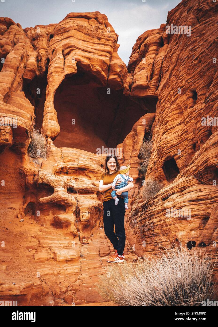A young woman with a baby is standing near red rocks in Valley of Fire ...