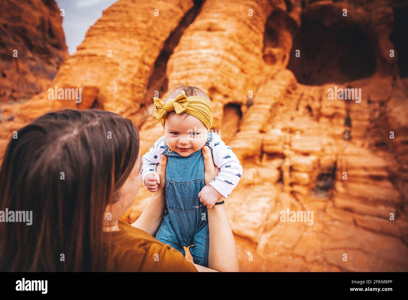 A young woman with a baby is standing near red rocks in Valley of Fire ...