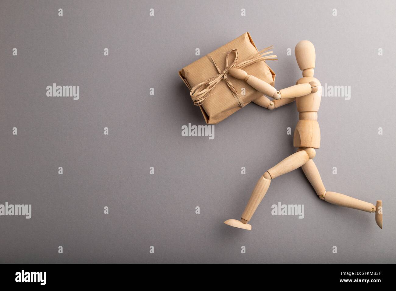Wooden mannequin holding a gift box on gray pastel background. copy ...