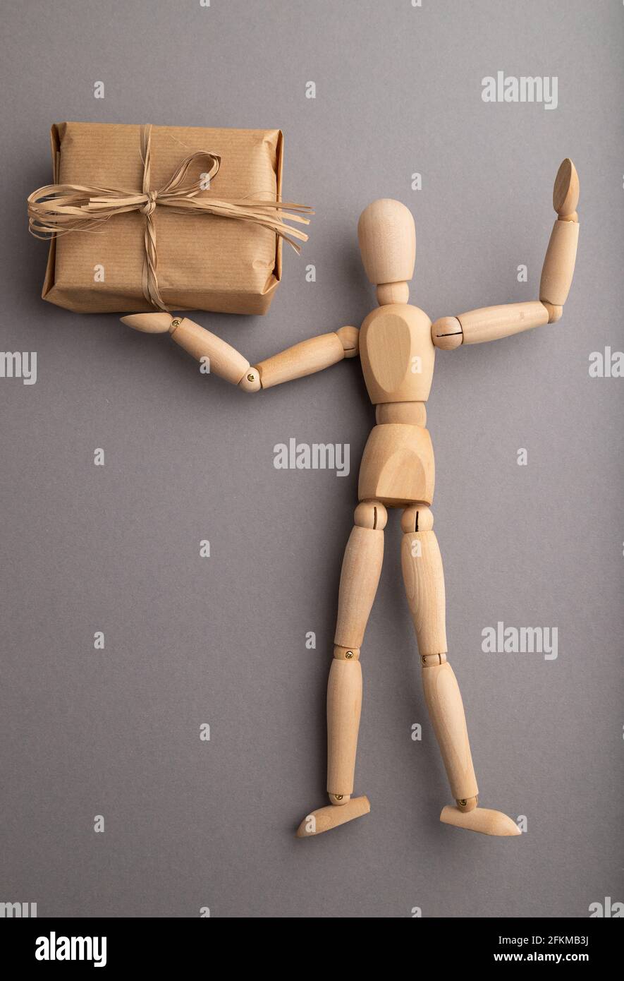 Wooden mannequin holding a gift box on gray pastel background. close up ...