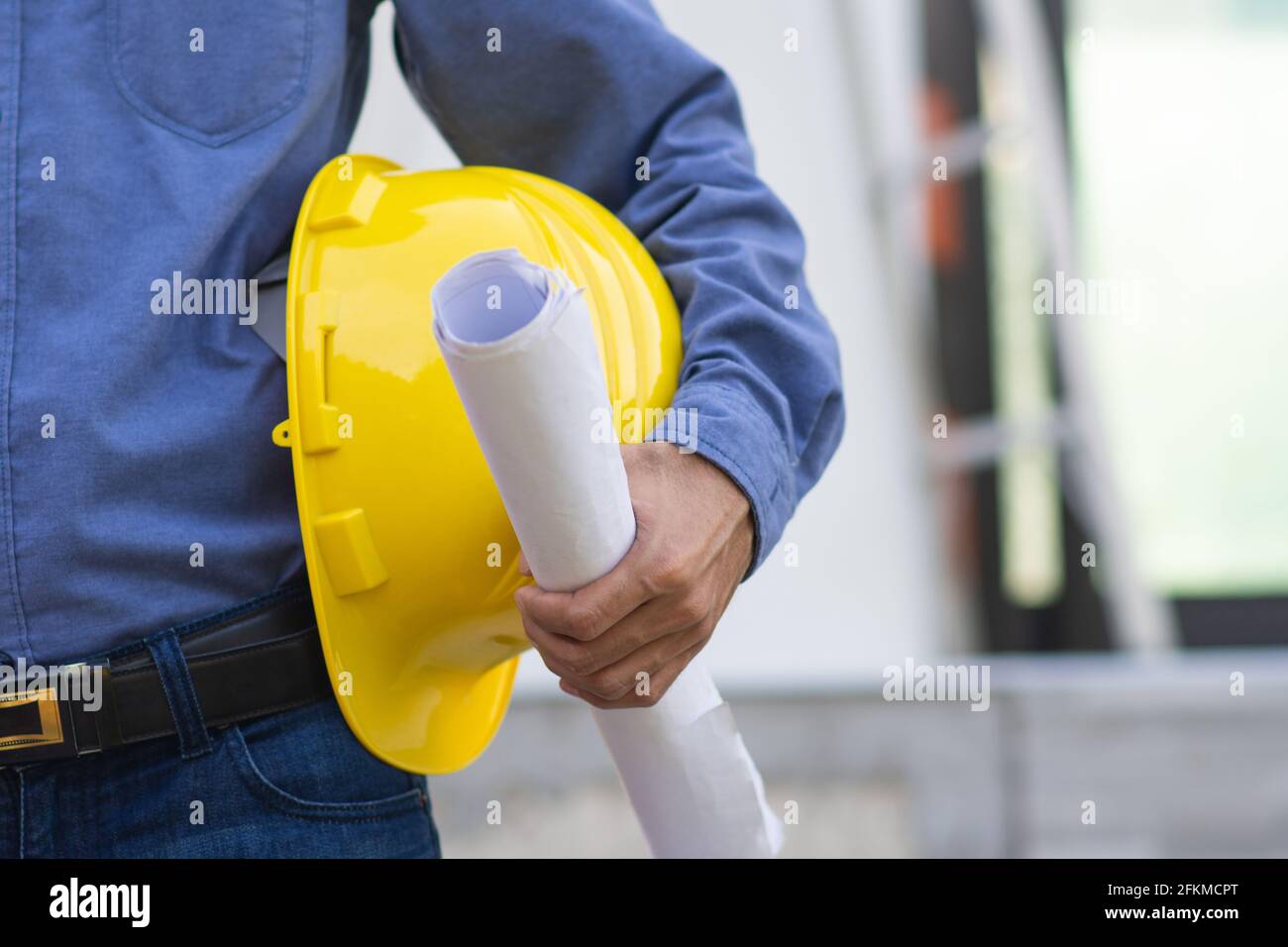 Engineer holding blueprint with yellow hard hat on site construction ...