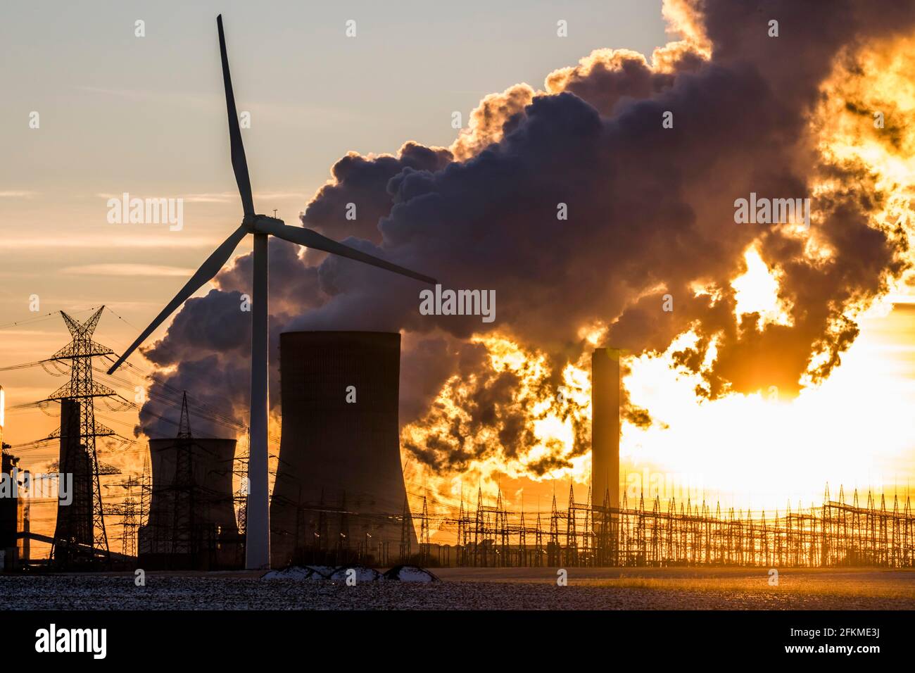 Wind turbine in front of steaming coal-fired power plant at sunset ...
