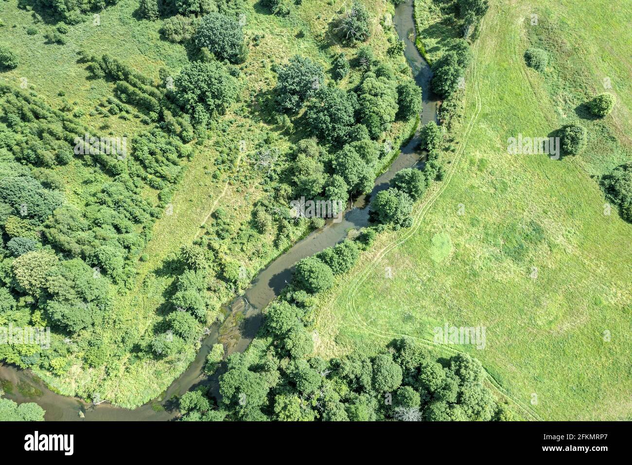 small river winding through green fields surrounded by mixed forests ...