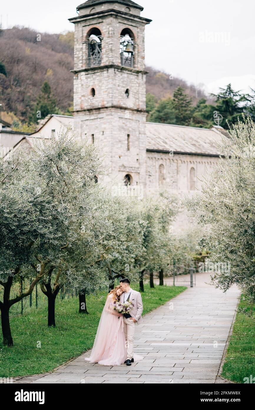 Newlyweds walk in an olive grove against the background of an old tower ...