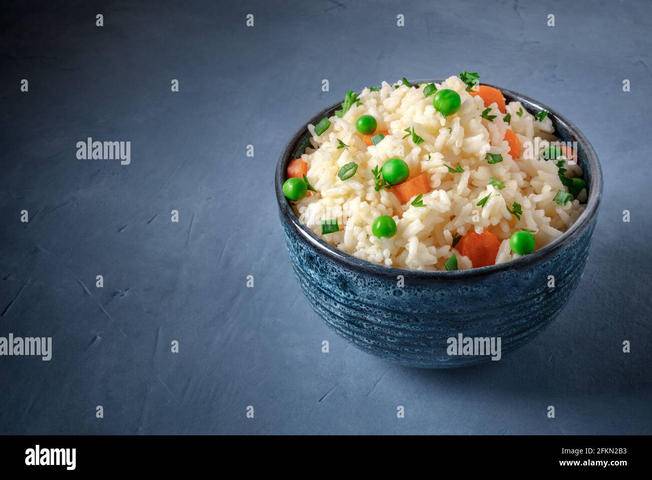 Rice with green peas, carrots, and scallions, on a dark blue background ...