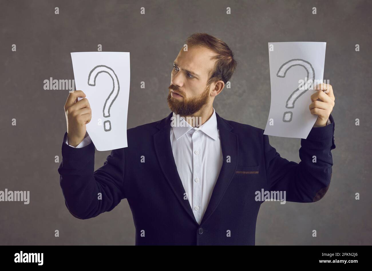 Puzzled businessman holding two question marks asking himself what ...