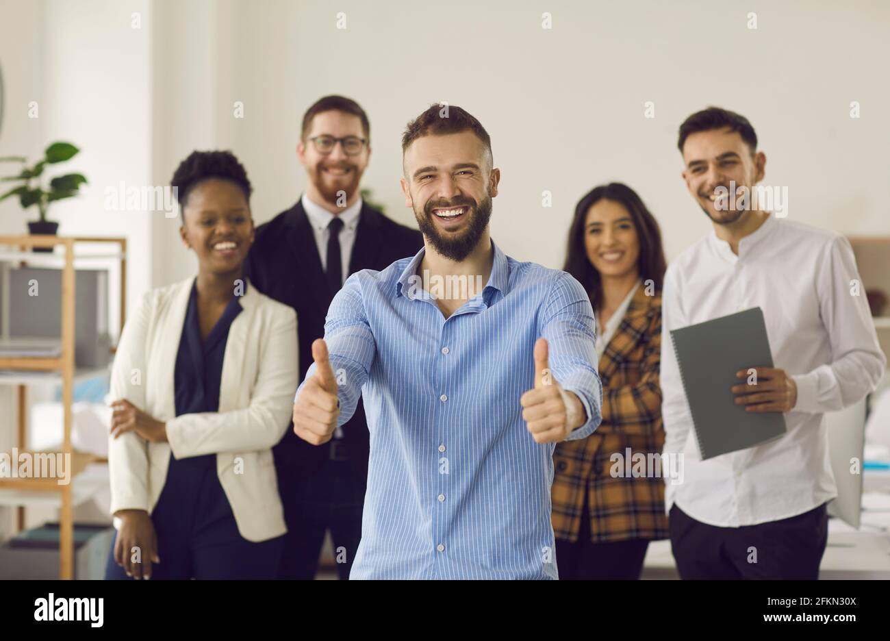 Smiling leader gesturing thumbs up standing with diverse business team ...