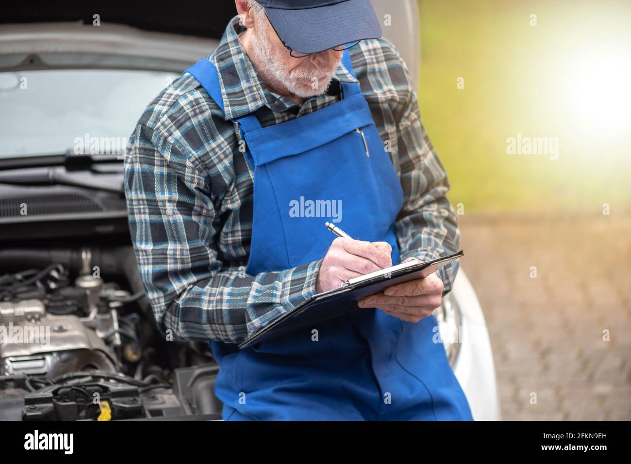 Car mechanic checking a car engine and writing on clipboard Stock Photo ...