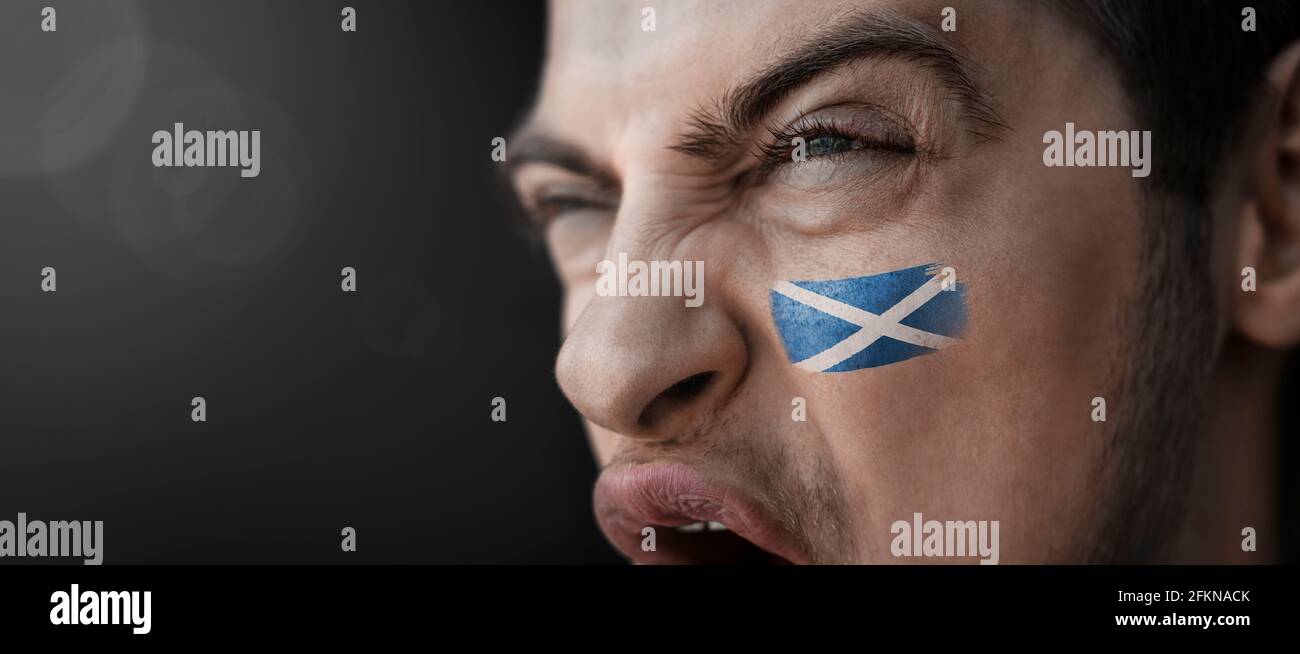 A screaming man with the image of the Scotland national flag on his ...