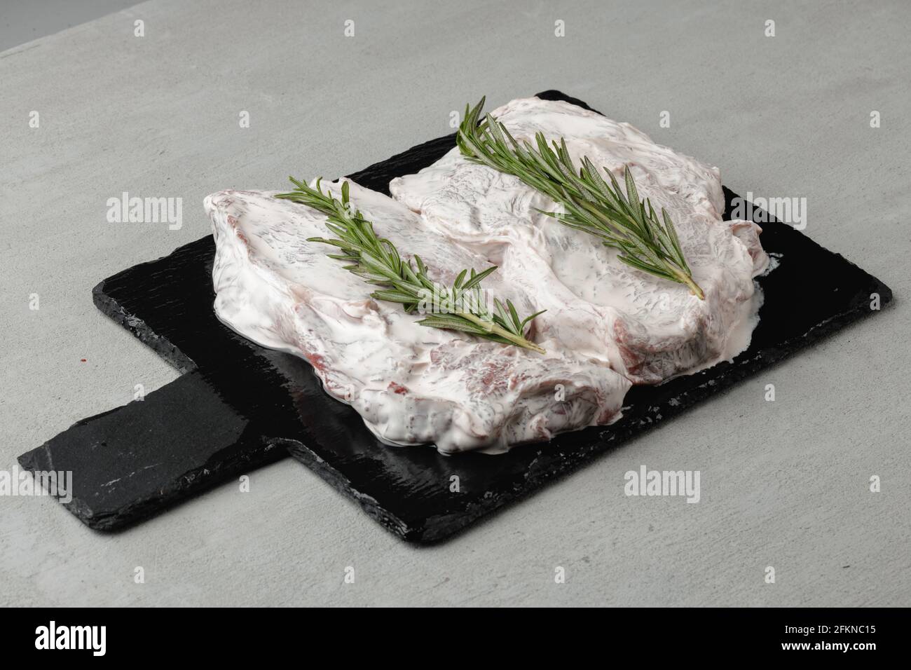 Marinated beef steaks with rosemary on black stone board Stock Photo ...