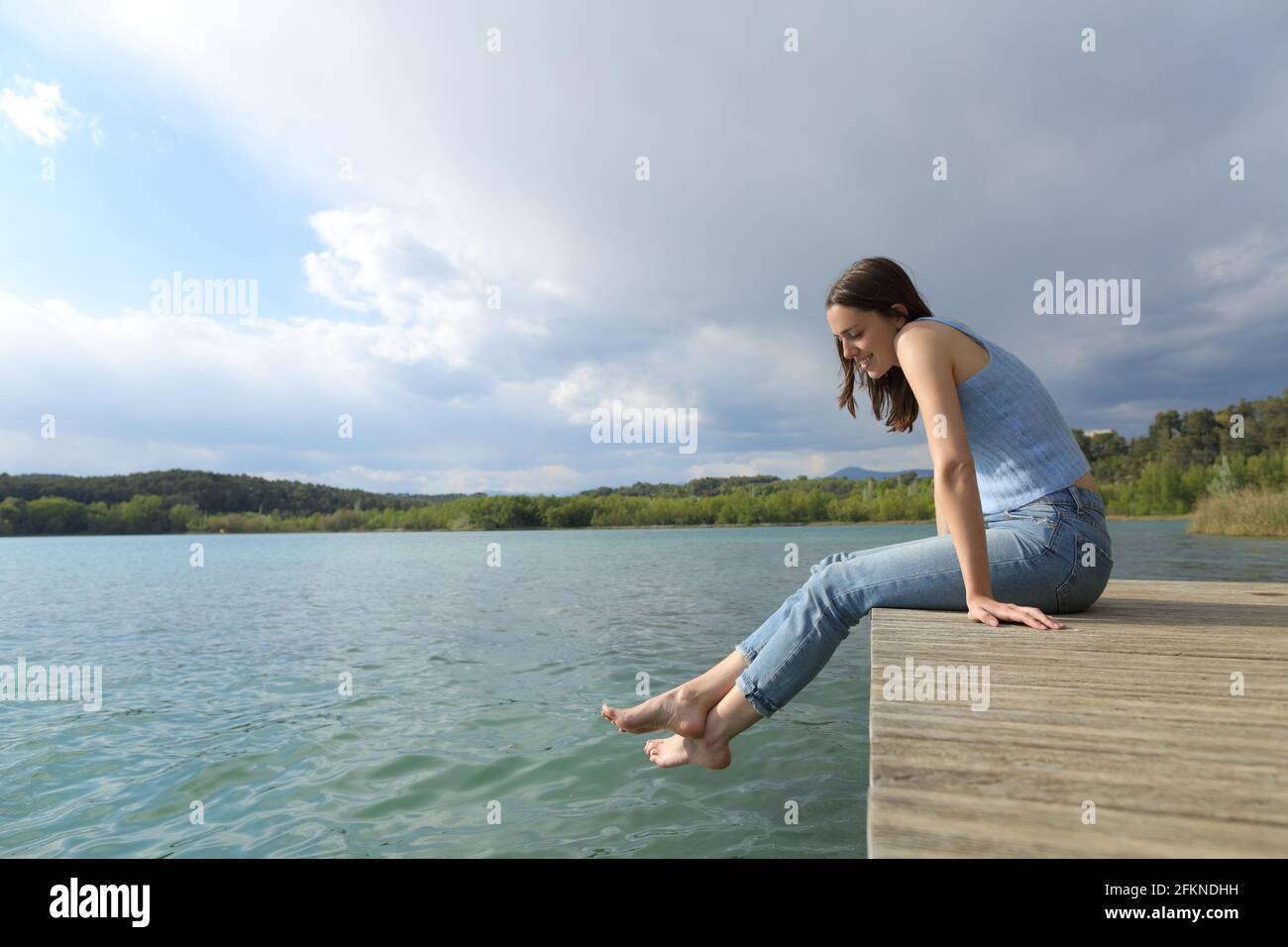 Full body profile of a happy woman resting sitting in a pier looking at ...