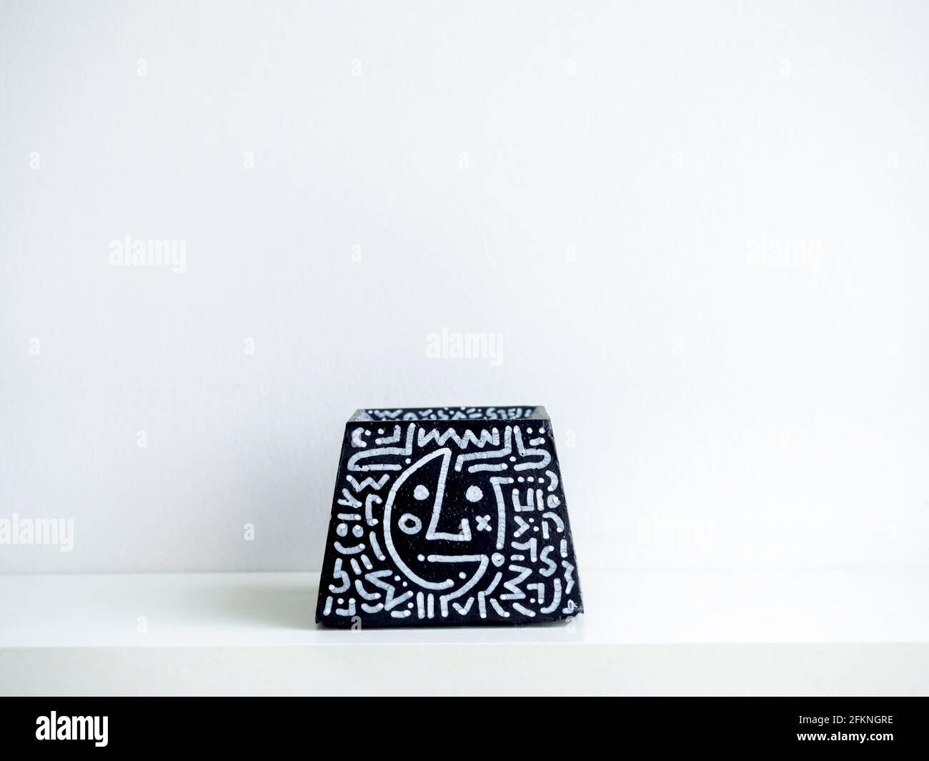 Empty DIY black concrete pot, pyramid shape with art drawing on a white ...