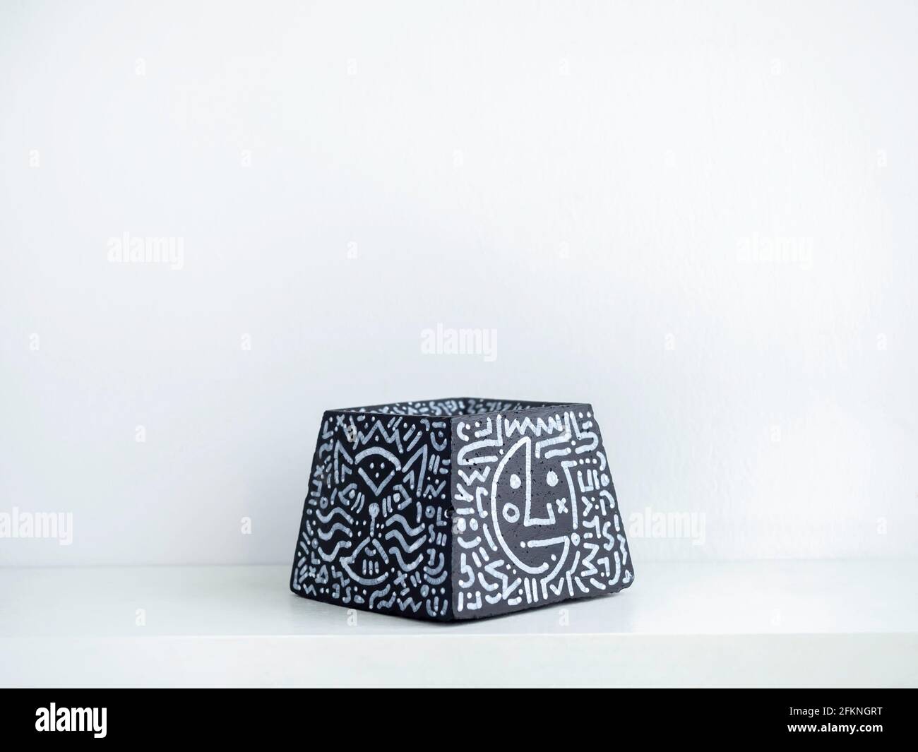 Empty DIY black concrete pot, pyramid shape with art drawing on a white ...