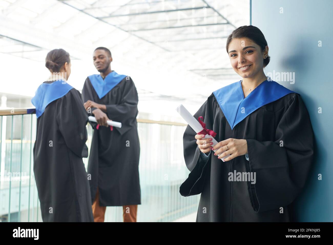 Group of young people wearing graduation gowns indoors in modern ...