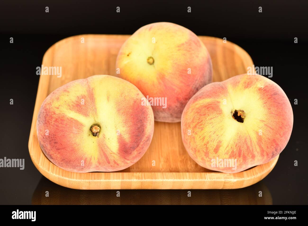 Three organic, sweet peaches on a bamboo tray, close-up, isolated on ...