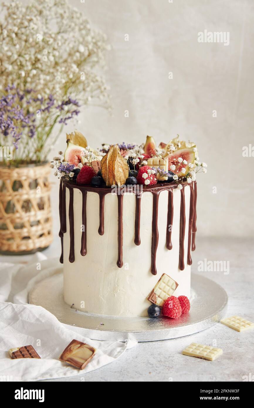 Elicious Boho Drip Cake with fruits and flowers on top on a white table ...