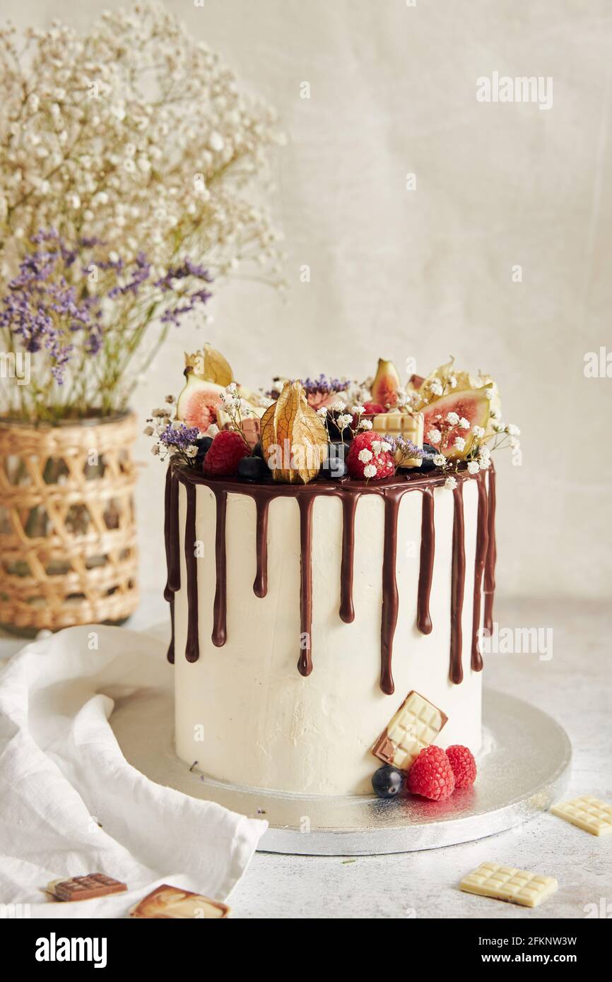 Delicious Boho Drip Cake with fruits and flowers on top on a white ...