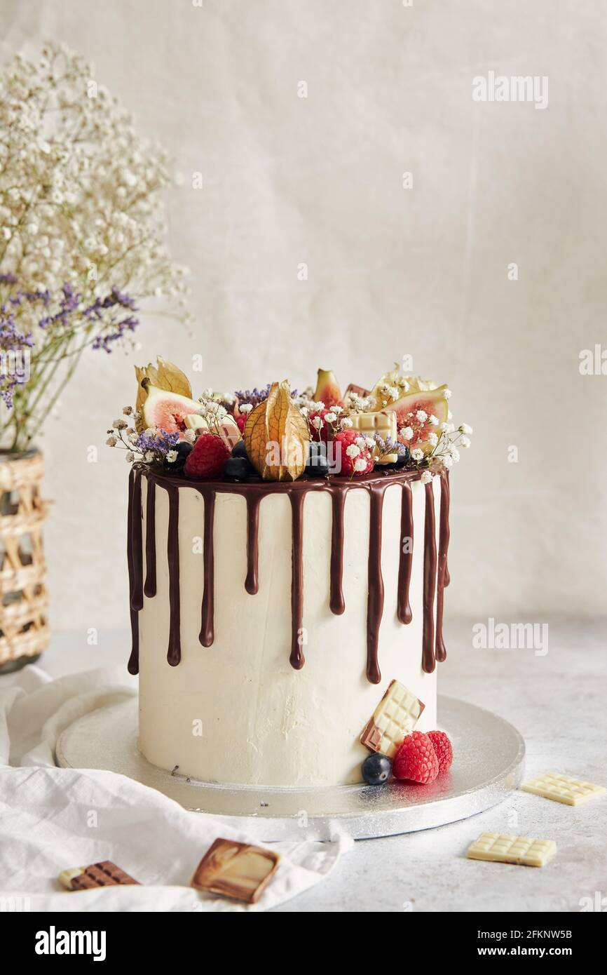 Delicious Boho Drip Cake with fruits and flowers on top on a white ...