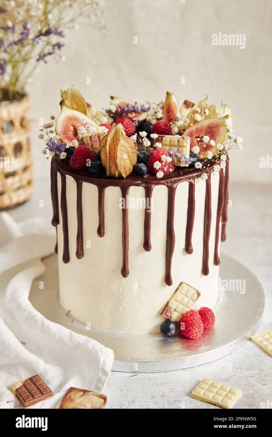 Delicious Boho Drip Cake with fruits and flowers on top on a white ...