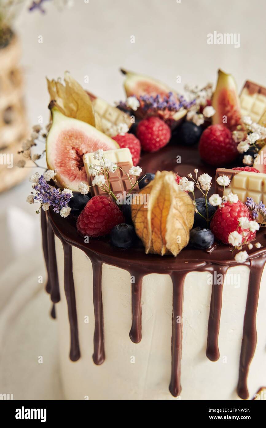 Delicious Boho Drip Cake with fruits and flowers on top on a white ...