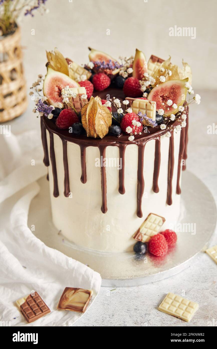 Delicious Boho Drip Cake with fruits and flowers on top on a white ...