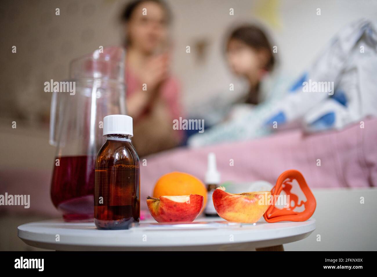 Jug with tea, medication syrup, fruit and inhaler on bedside table ...
