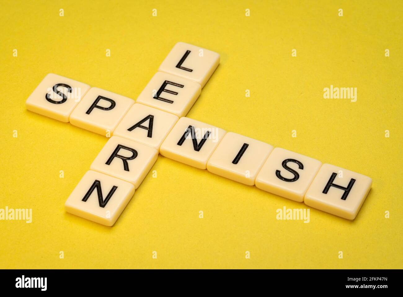 learn Spanish crossword in ivory letter tiles against yellow textured ...