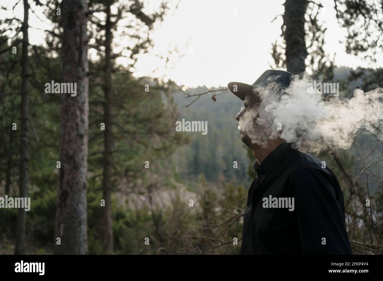 Cowboy smoking in the forest.Male in black hat and dark shirt with ...