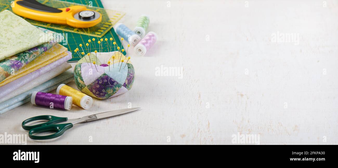 Pincushion, stack of fabrics, sewing and quilting accessories lying on ...
