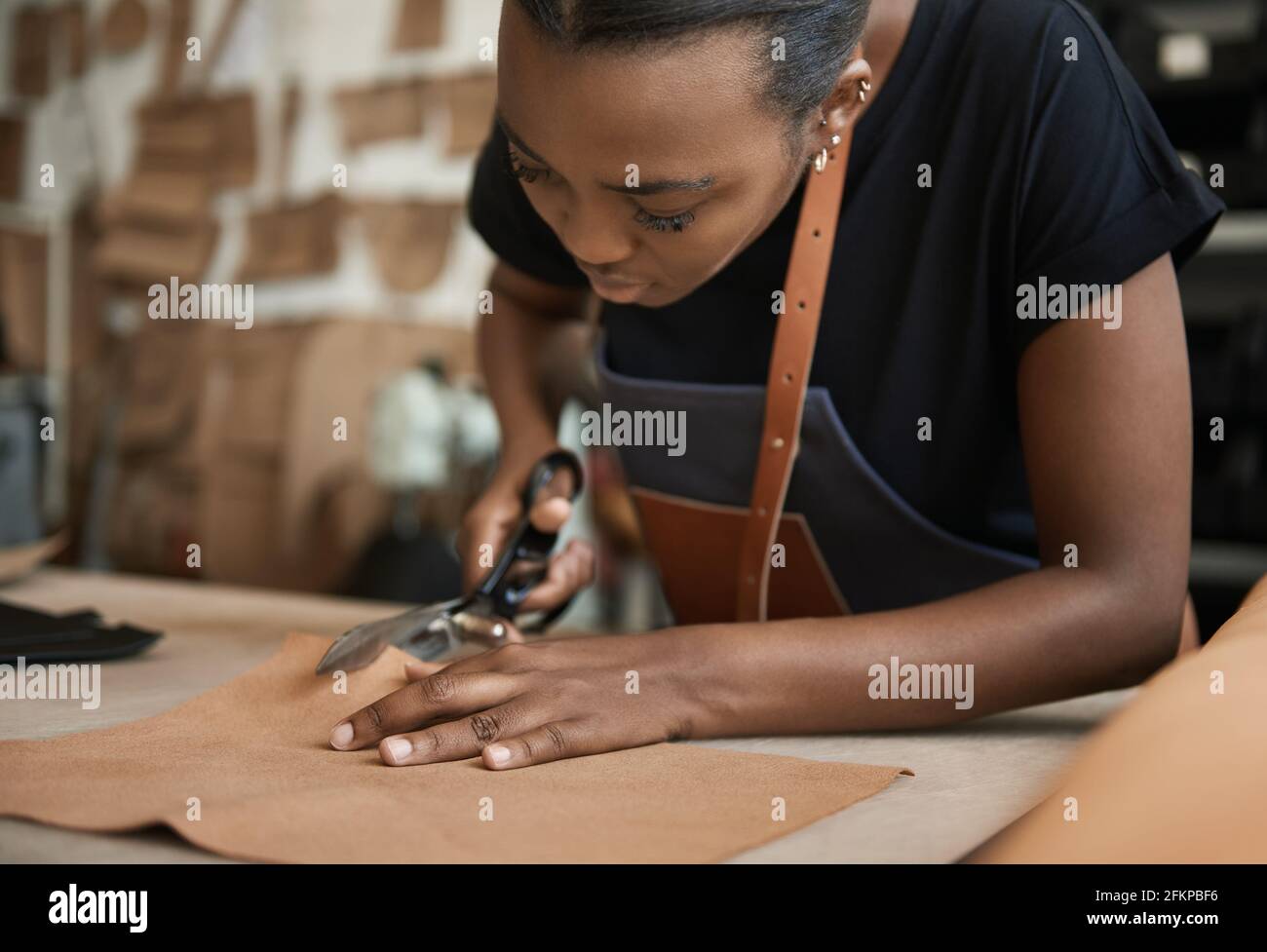 Young African female artisan cutting leather at a workbench Stock Photo ...
