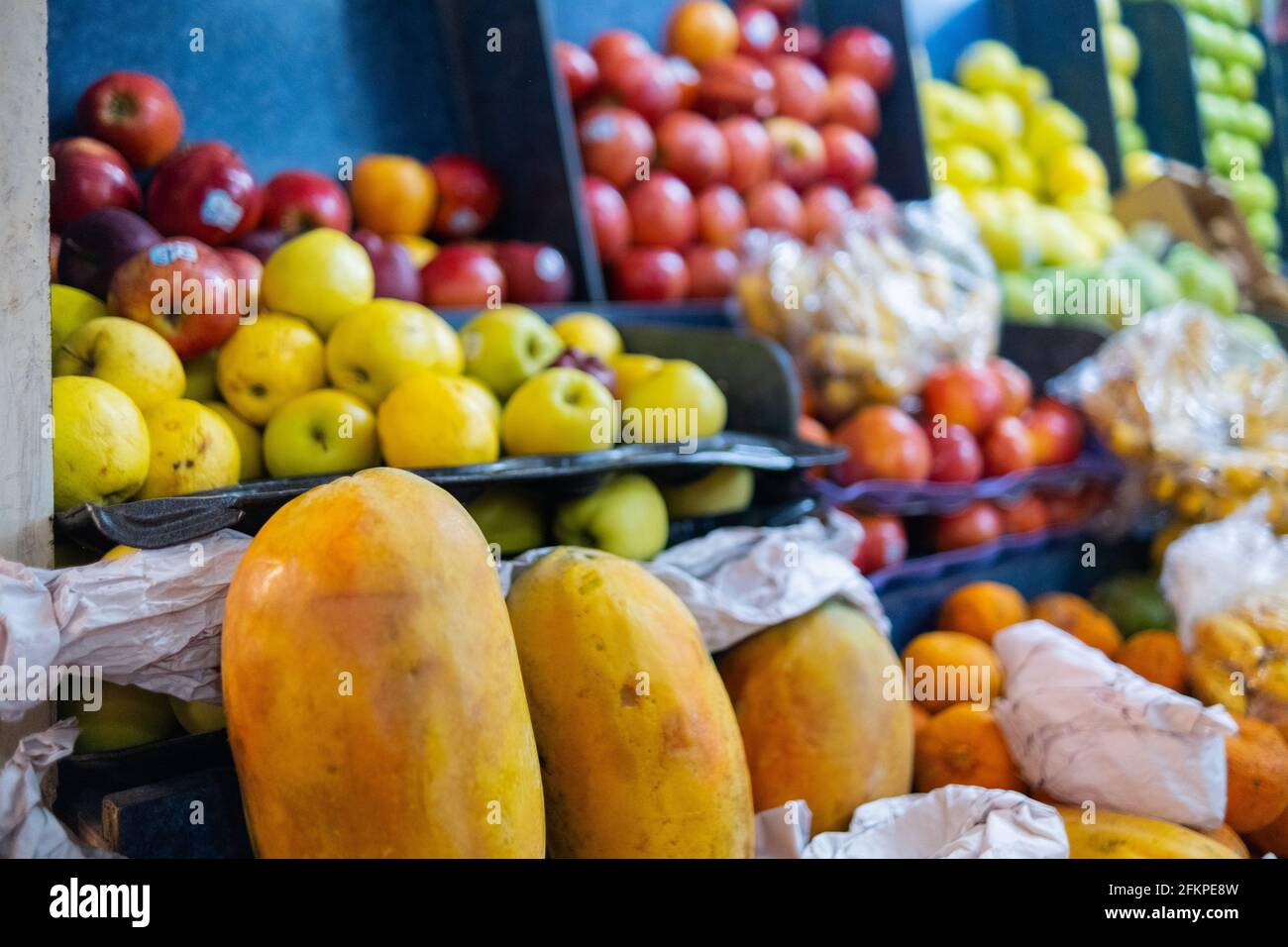 Colorful fruit stand with papayas, red and yellow apples, and more ...