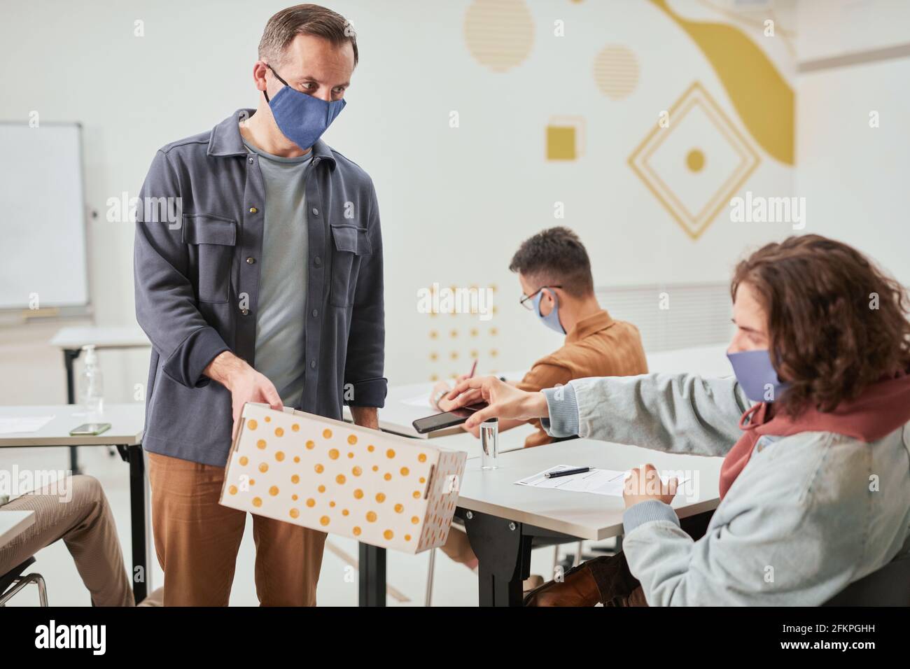 Portrait of male teacher collecting smartphones in school classroom ...