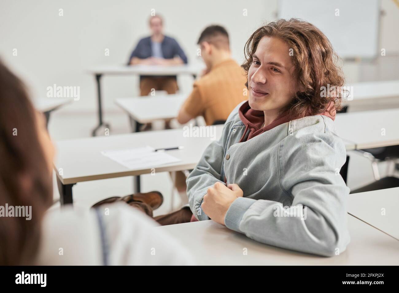 Portrait of smiling teenage boy talking to friends during lecture in ...