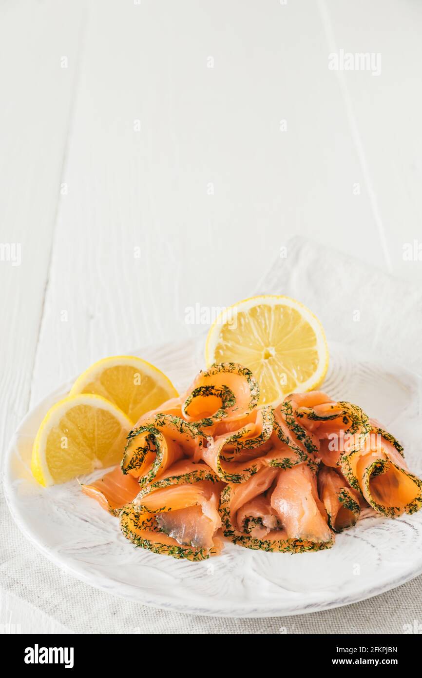 Smoked salmon rolls with lemon on white plate on white wooden ...
