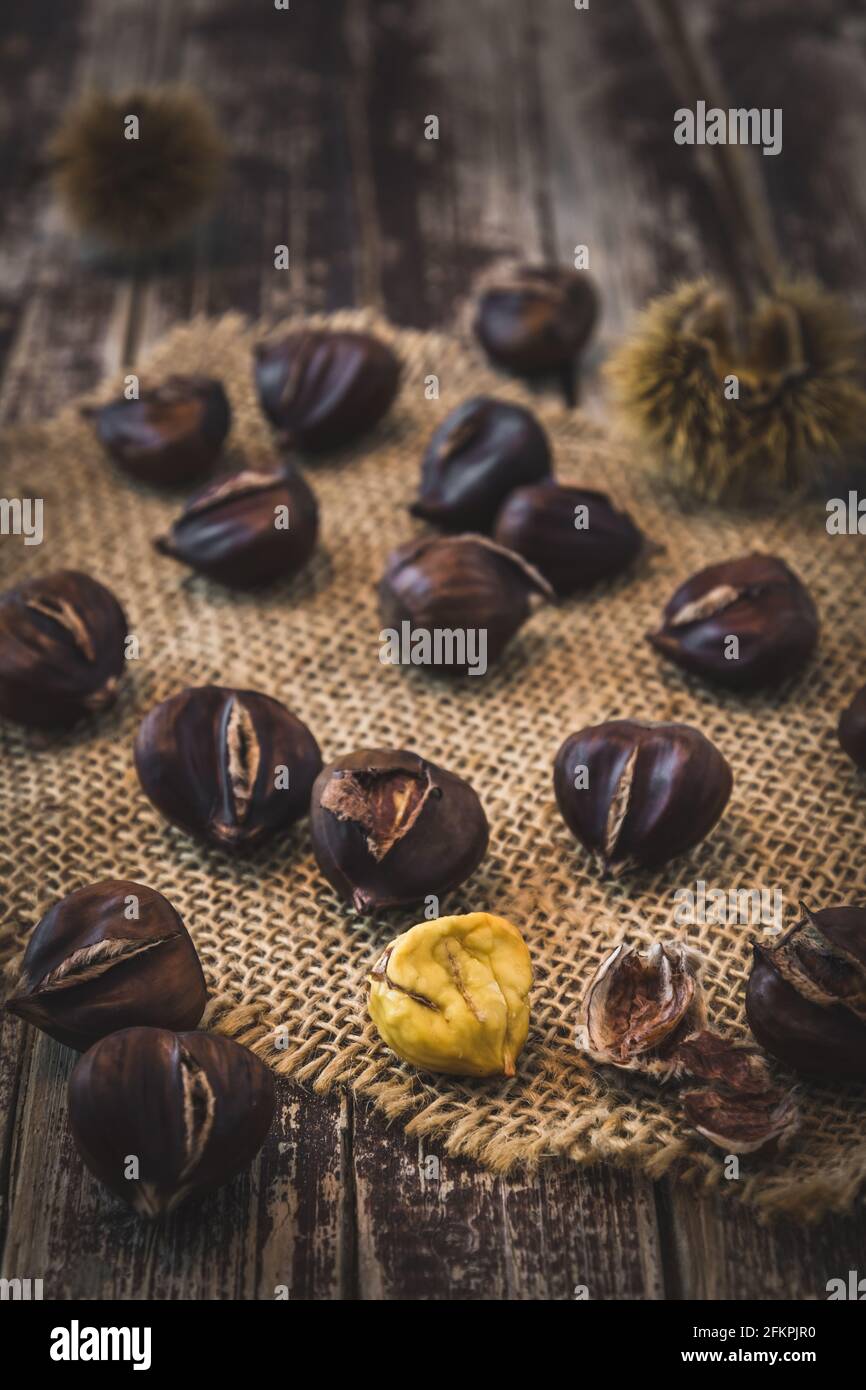 Roasted chestnuts, one peeled, on a dark wooden background, vertical ...