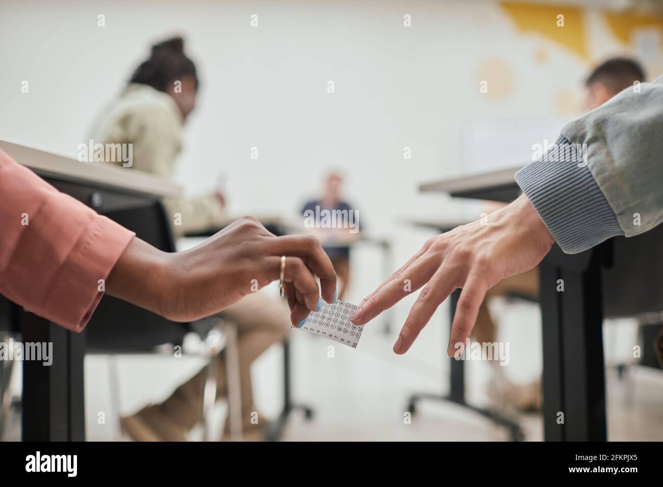 Close up of two unrecognizable students passing cheat note while taking ...