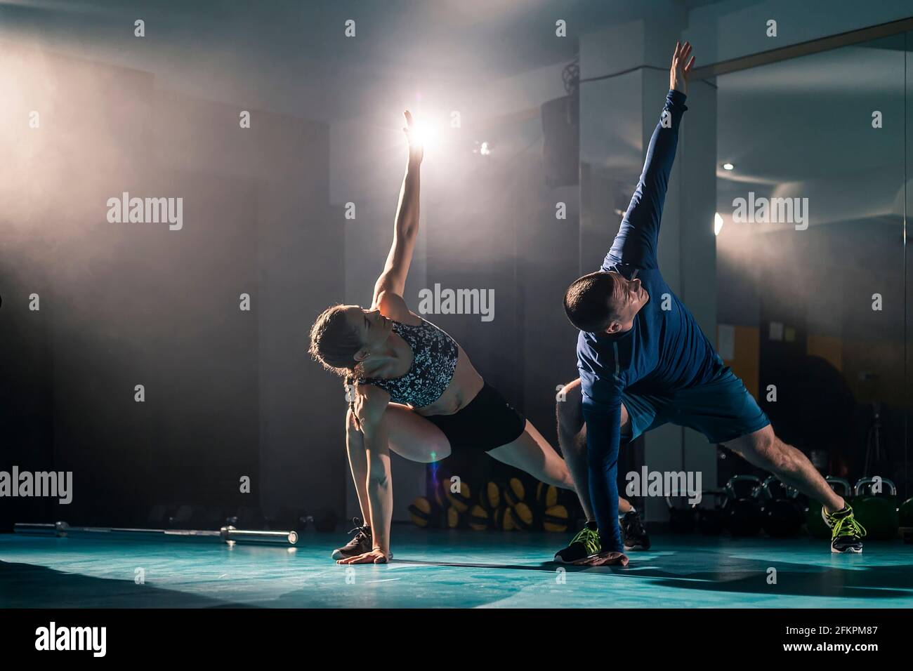 Woman and a man stretching in the gym through an exercise in a sideways ...