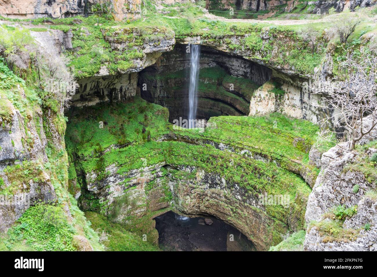 Waterfall behind a natural bridge covered in lush green vegetation ...