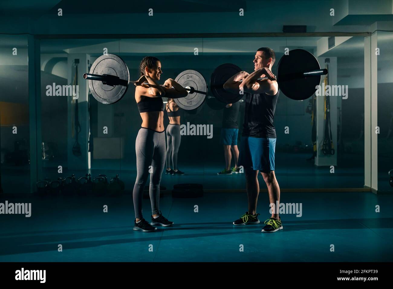 A fit couple standing in the gym with weights on and doing an exercise ...