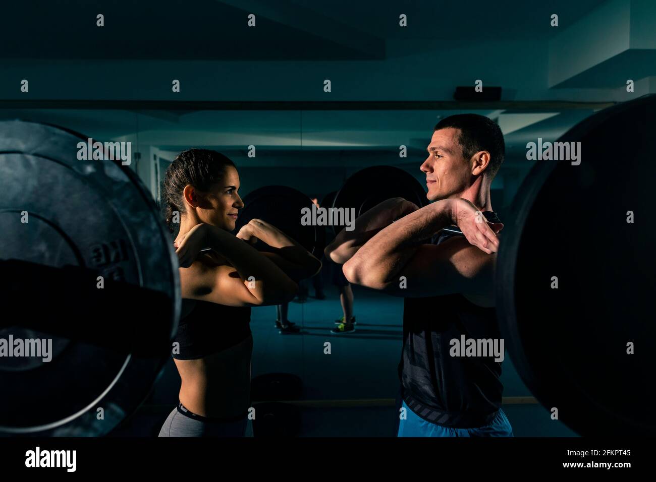 A fit couple standing in the gym with weights on and doing an exercise ...