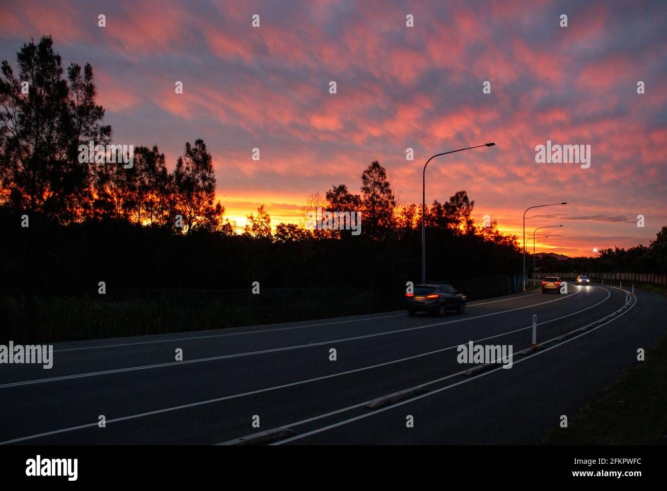 Scenic view of a curved road with cars passing under a beautiful sunset ...