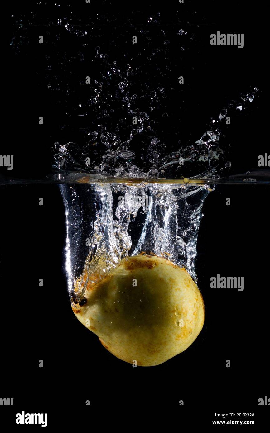 Vertical shot of a pear in water with splashes on a dark isolated ...