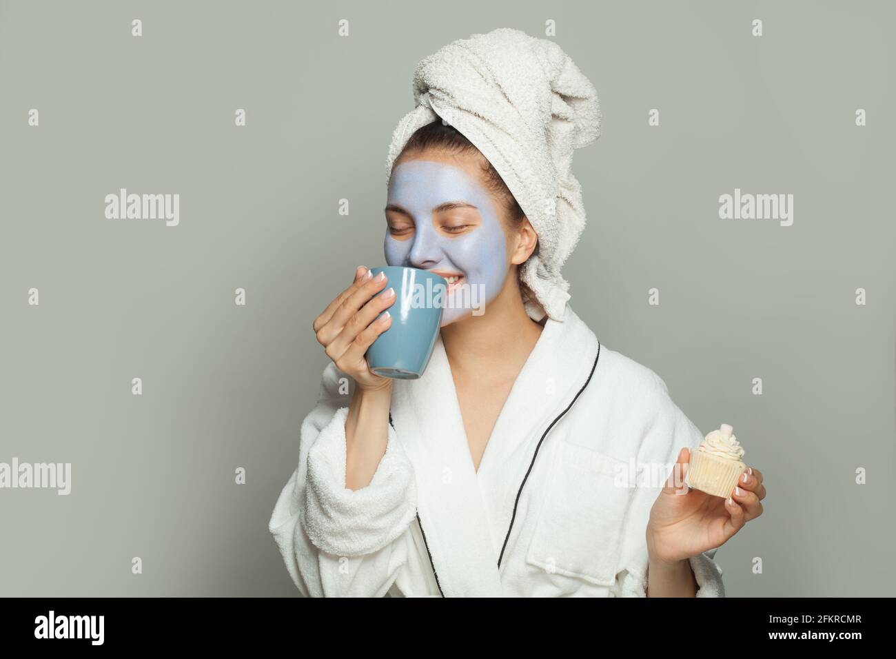 Smiling spa model woman in cosmetic face mask eating breakfast and ...