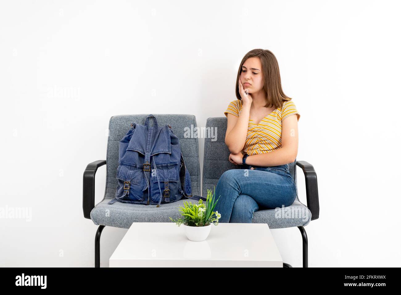 Worried young female client in the waiting room sitting on a gray chair ...