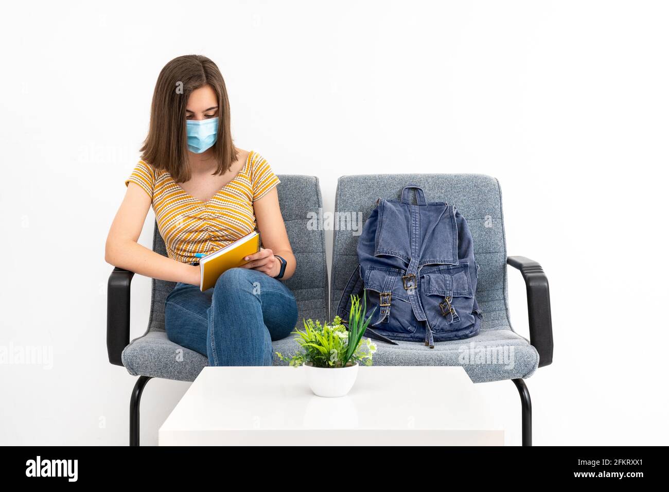 Young female client in the waiting room with a mask studying while ...