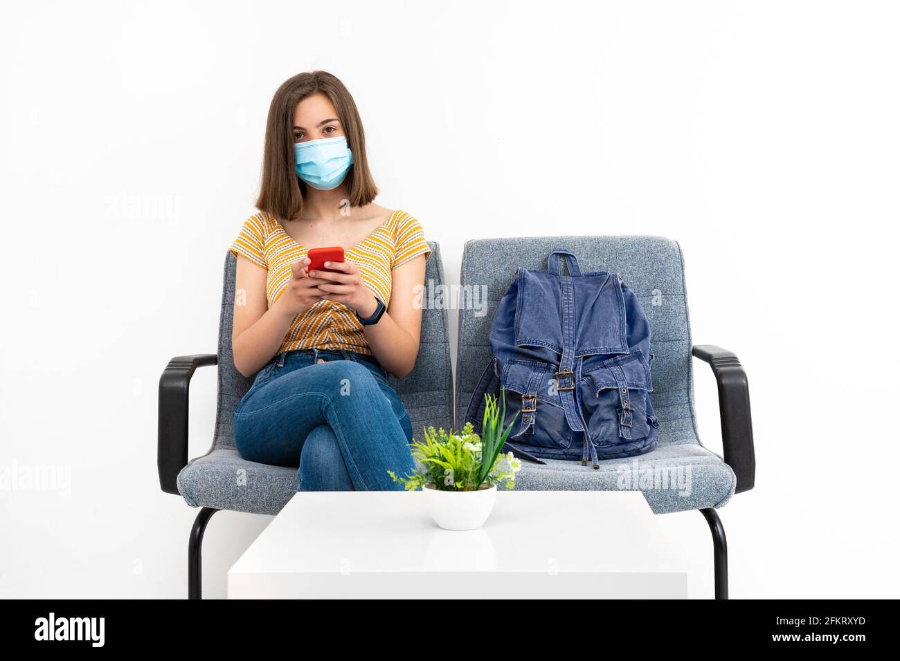 Young female client in the waiting room with a mask and her phone ...