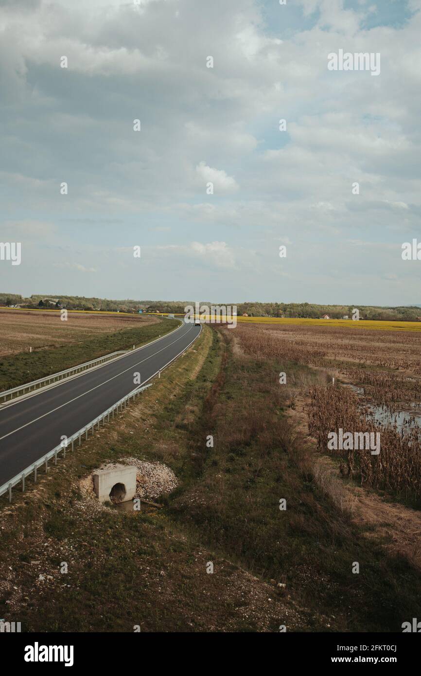 Vertical shot of a long empty road running along a dry field of grass ...
