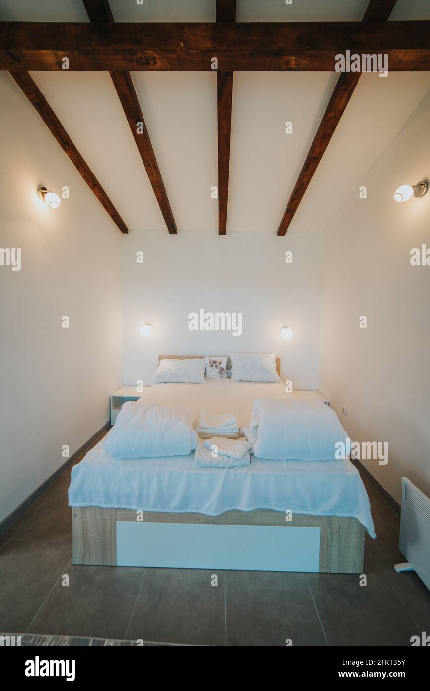 Vertical shot of a modern attic room with a white kin-size bed and ...